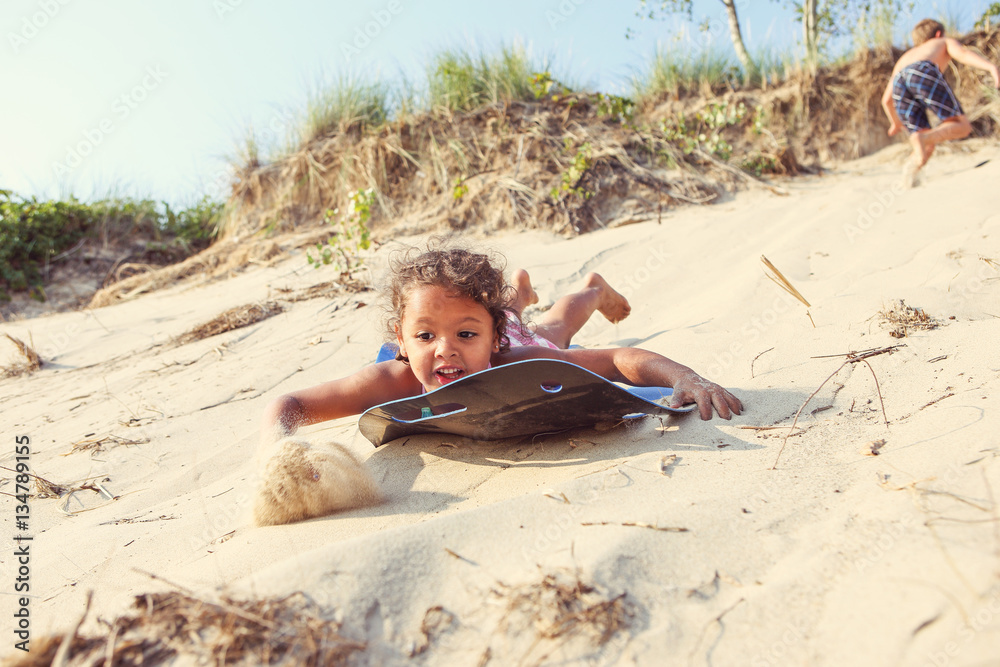 Young girl sliding down a sand dune on a sled in the summer. Som Stock ...