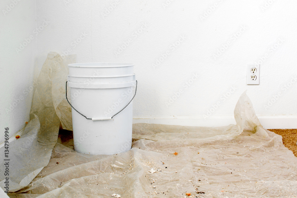 A white bucket over a sheet of plastic placed over carpet floor to ...