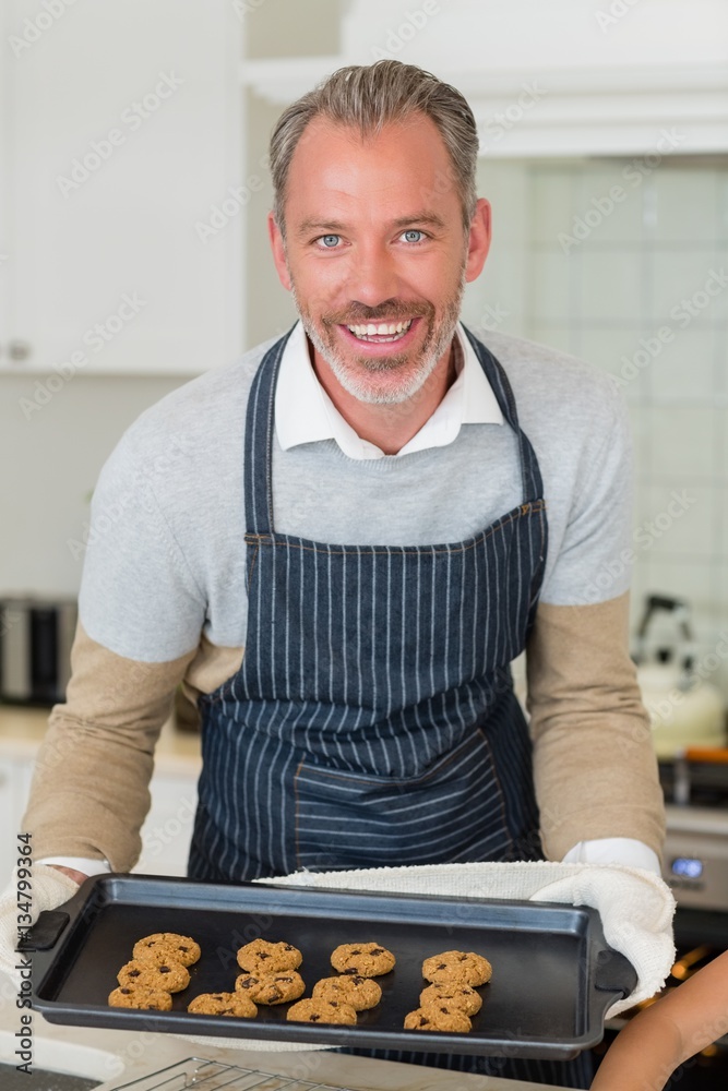 Foto Stock Man holding a cookies in baking tray at kitchen | Adobe Stock