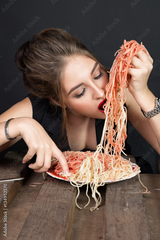 Woman eating pasta at wooden table. Fashionable young woman holding ...
