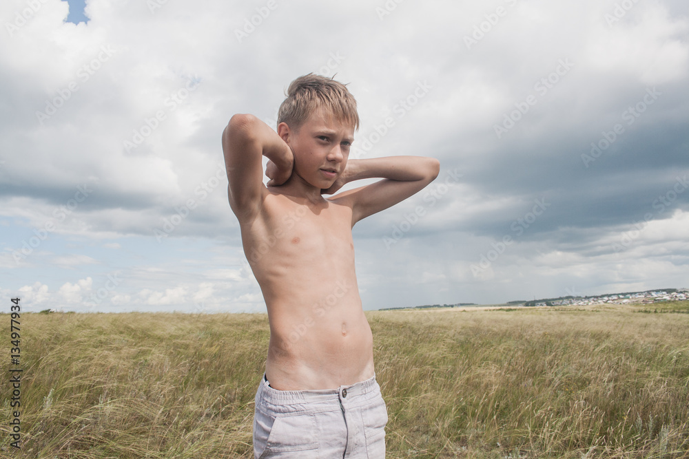 young boy stands in a field. boy in shorts. boy stands in the desert ...