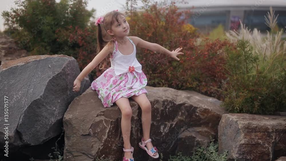 Vidéo Stock little girl sitting on a large rock in nature sings and ...
