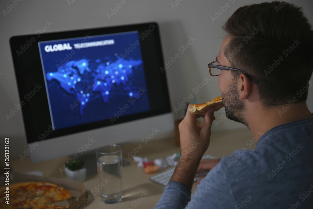 Man eating pizza while working with computer late in evening, close up ...