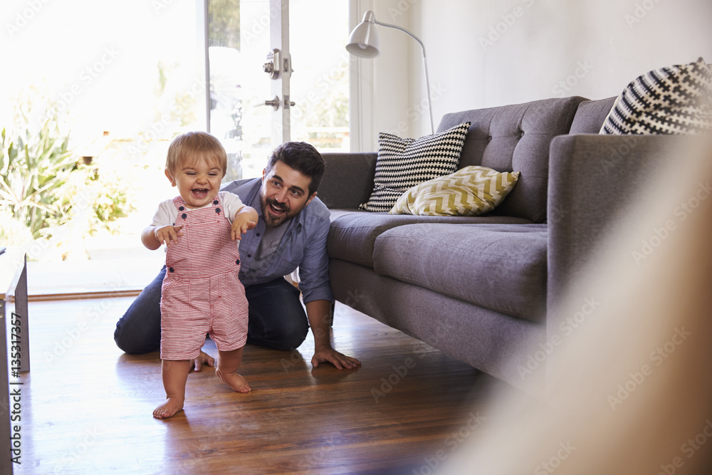Parents Watching Baby Daughter Take First Steps At Home Stock Photo ...