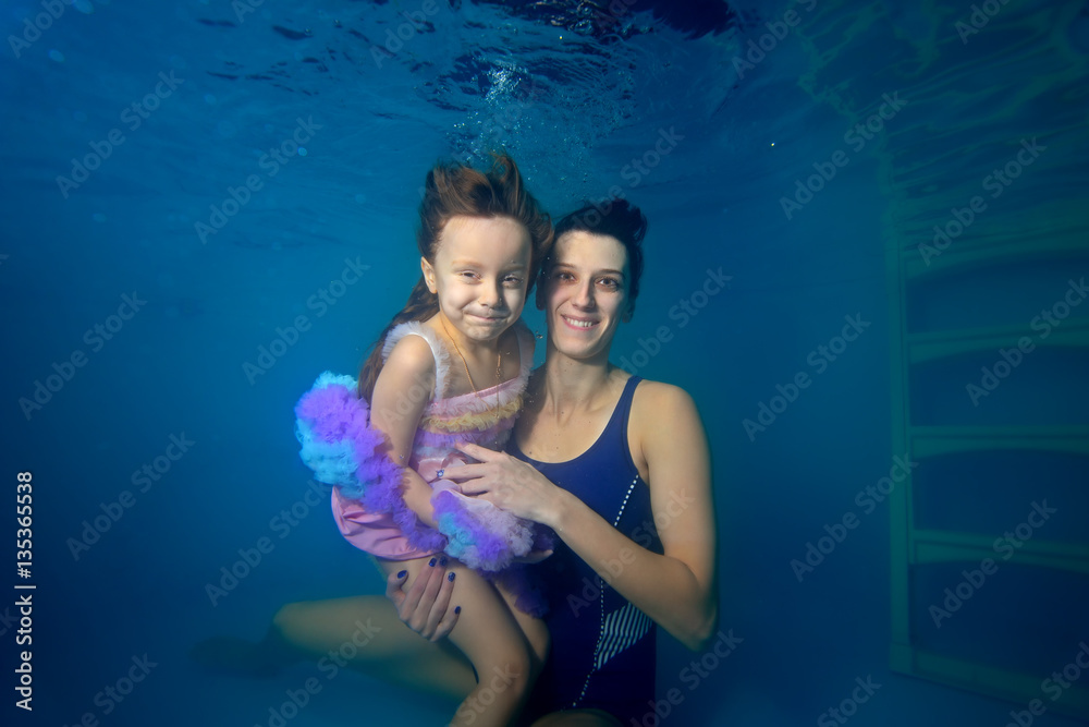 Little girl in a beautiful dress swims and poses with mom underwater on ...