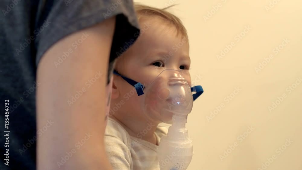 Close view of little baby with inhaler mask on his face over mother's ...