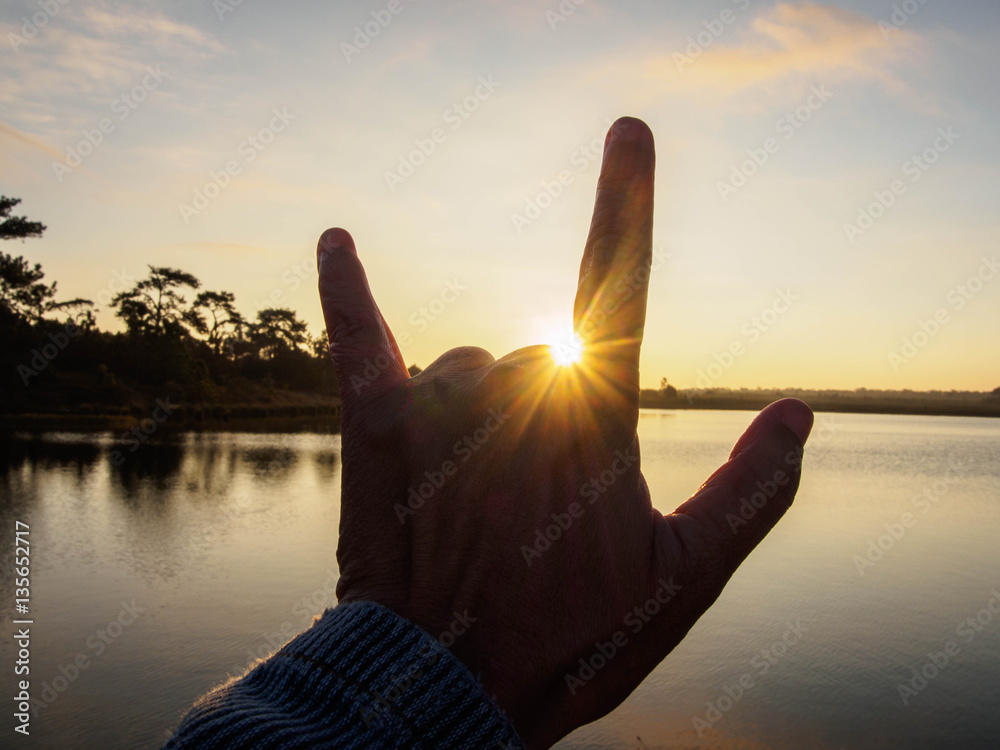 hand symbol against sunlight at sunrise near the pond on the mountain ...