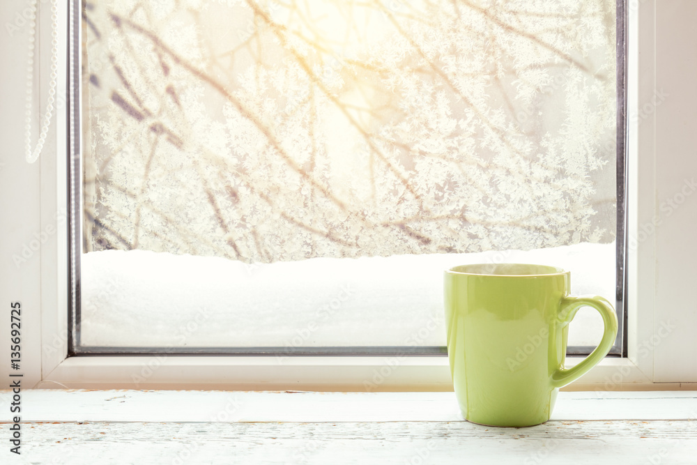 Cup of coffee on the window sill. In the background frosty pattern on ...