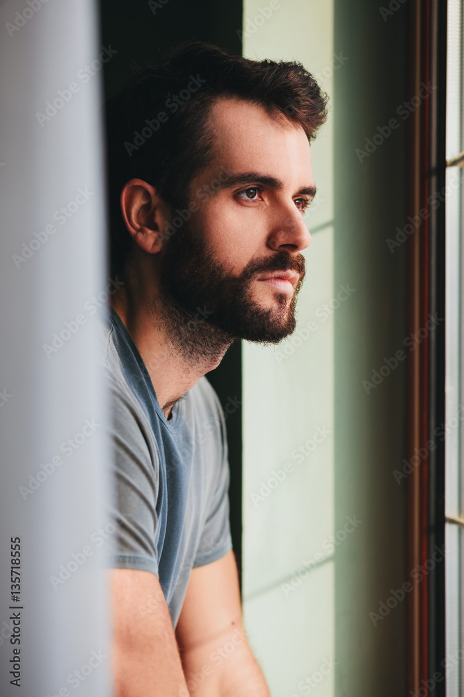 Young man standing by the window looking outside Stock Photo | Adobe Stock