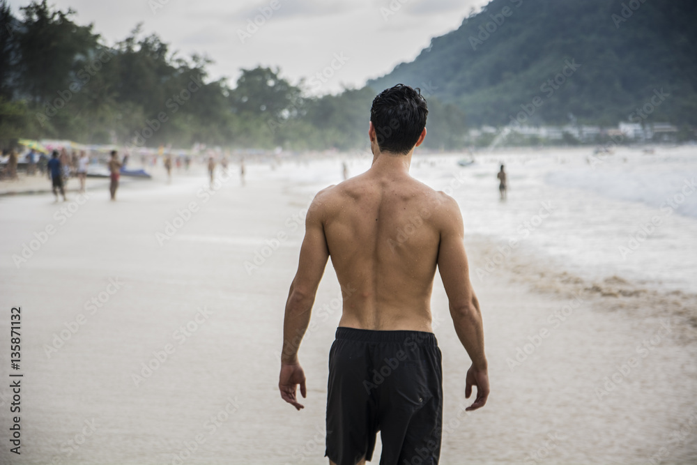 Half body back shot of a handsome young man standing on a beach in ...