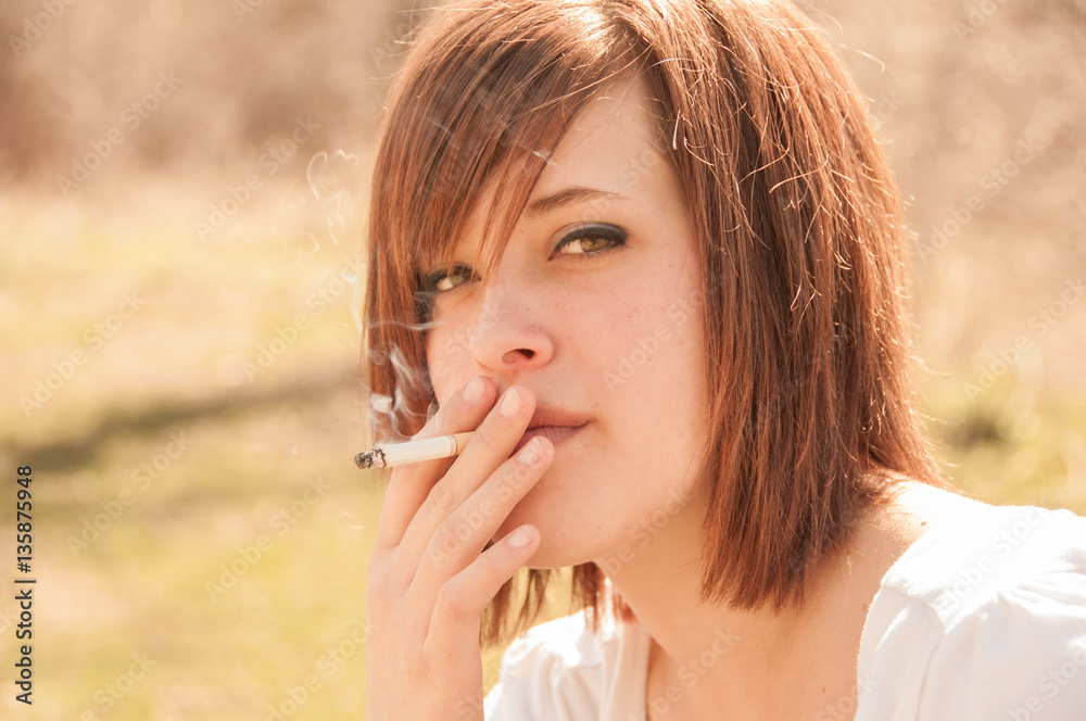 Teenager smoking. Caucasian girl looks at the camera whilst smoking a ...