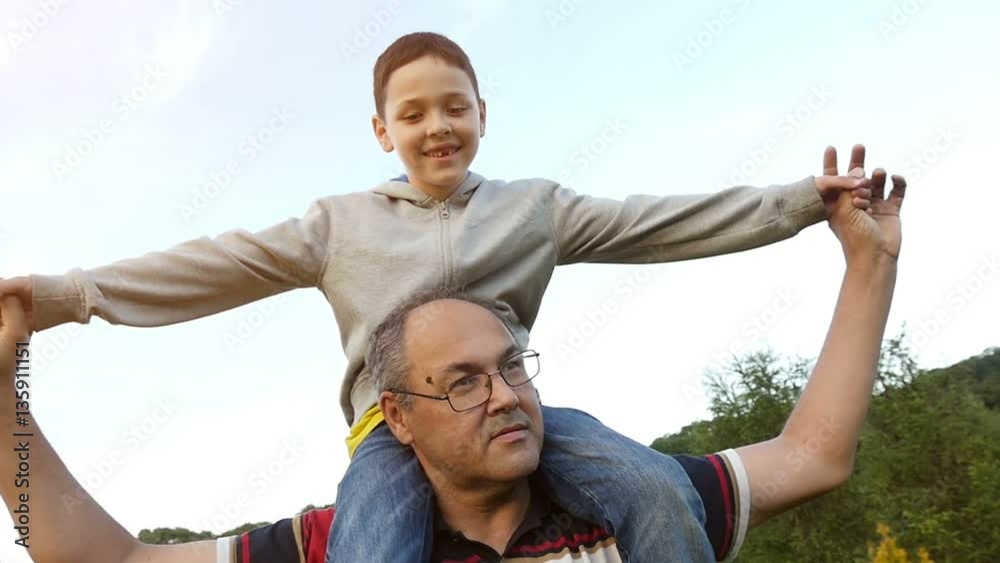 Funny man with a boy on his neck turning left and right in park. Slow ...