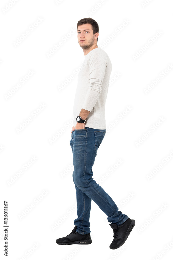 Side view of casual man in jeans and light gray shirt walking and ...