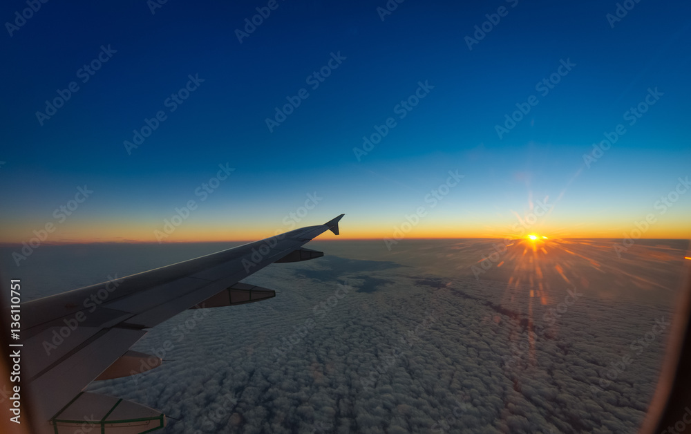 aircraft window view of wing with setting sun and deep blue sky and ...