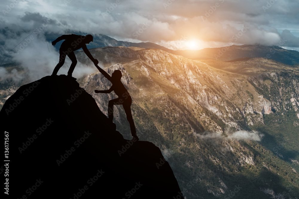 Male and female hikers climbing up mountain cliff and one of them ...