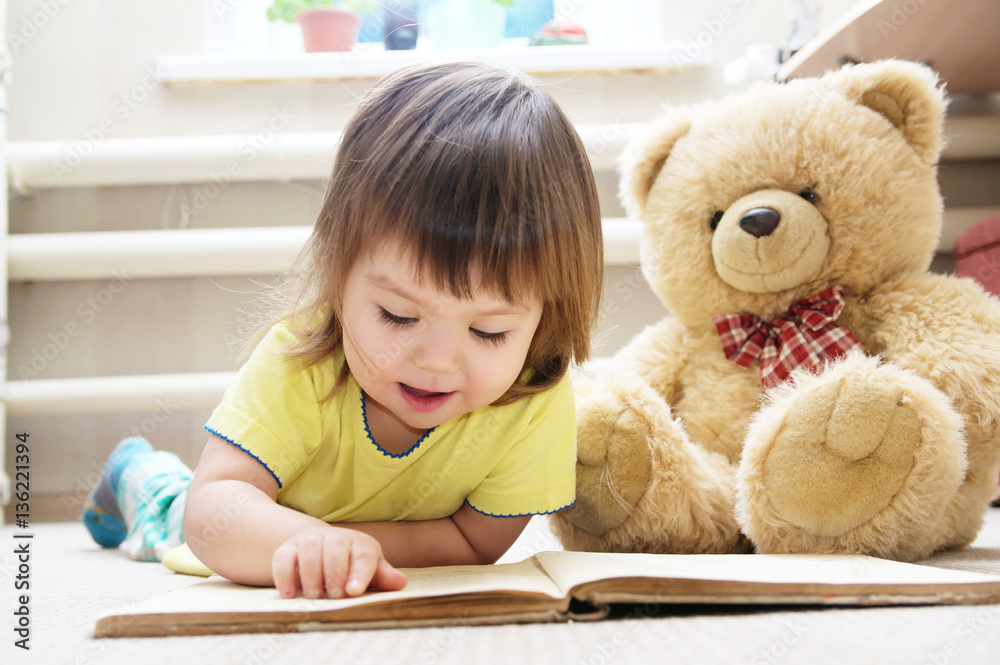 little girl reading book lying on stomach in her room on carpet with ...