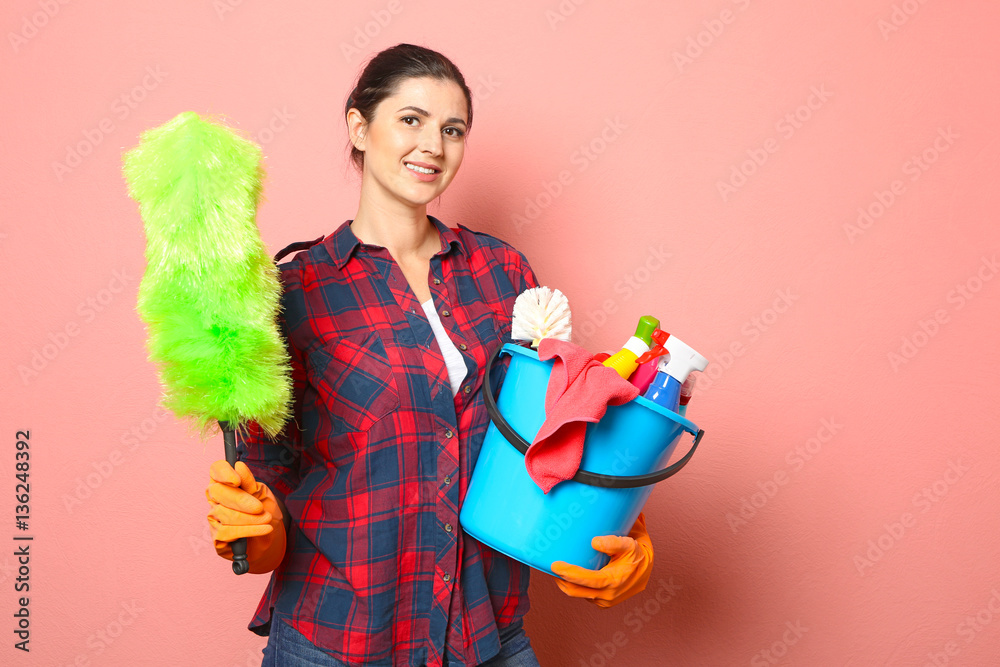 Young beautiful woman with cleaning tools in bucket on pink background ...