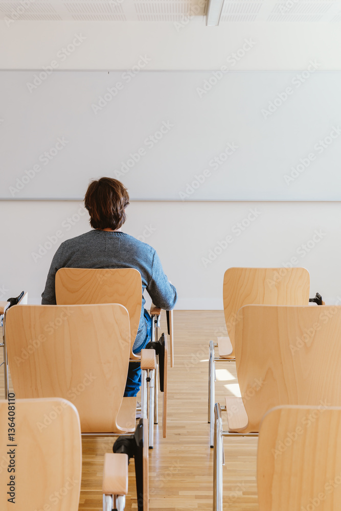 Back view of man sitting in the classroom alone. Vertical indoors shot ...