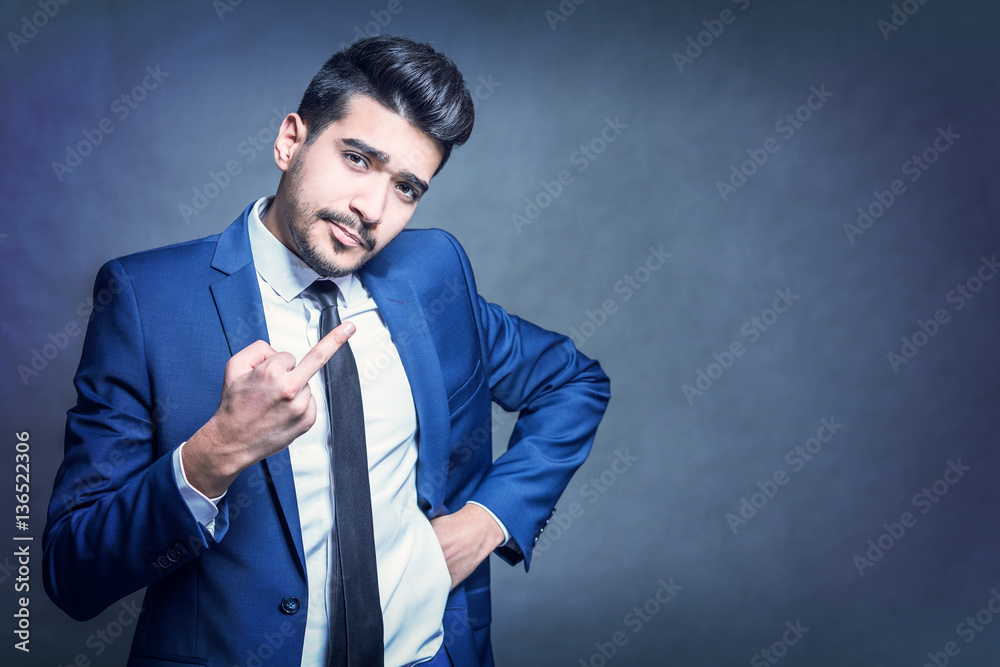 Young attractive man in a blue suit showing middle finger on a blue ...