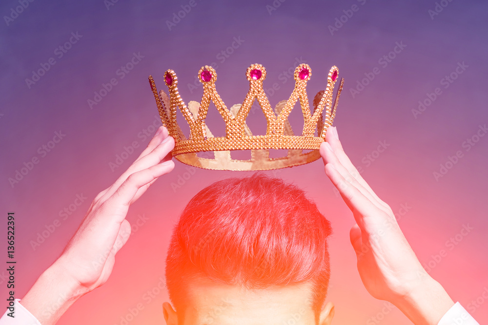 Man brunette holding above his head a golden crown in the bright glow ...