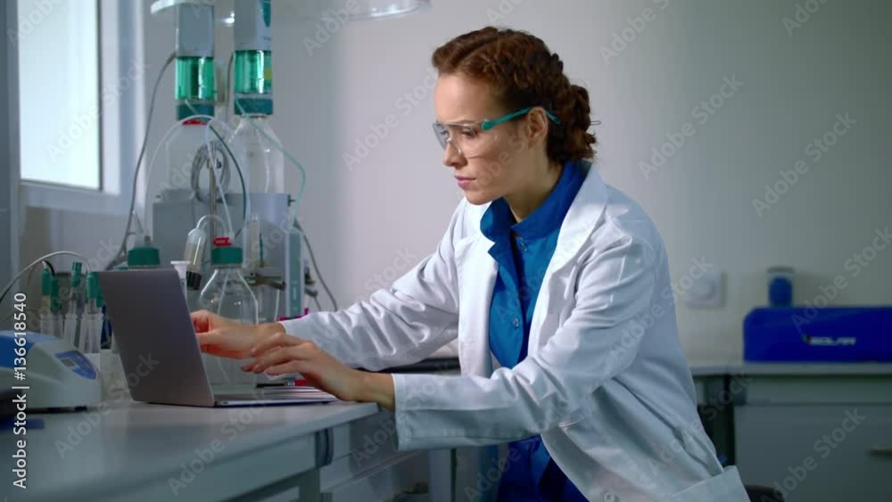 Female scientist working in laboratory. Lab worker typing test report ...