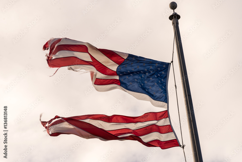 American flag torn down the middle waving in the wind on a cloudy sky ...