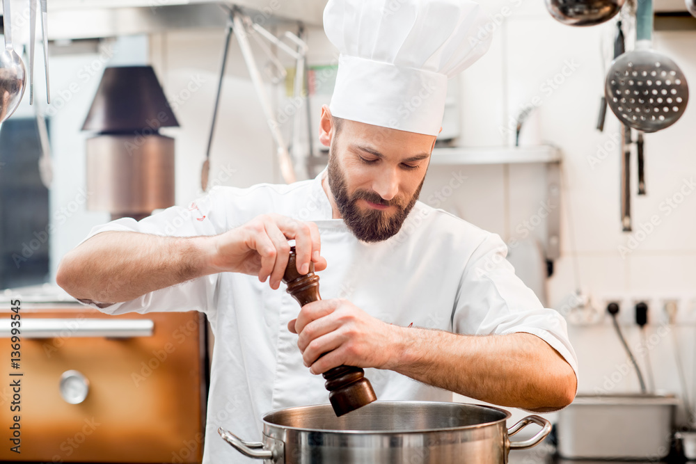 Chef cook in uniform peppering soup in the big cooker at the restaurant ...