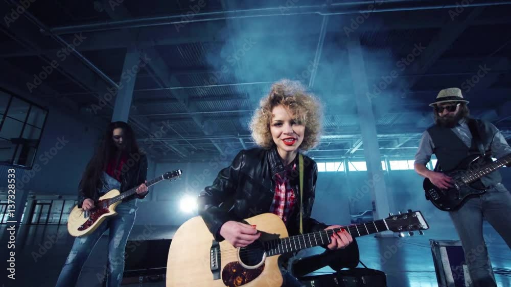 Low angle camera quickly zooming in shooting rock band playing guitars ...