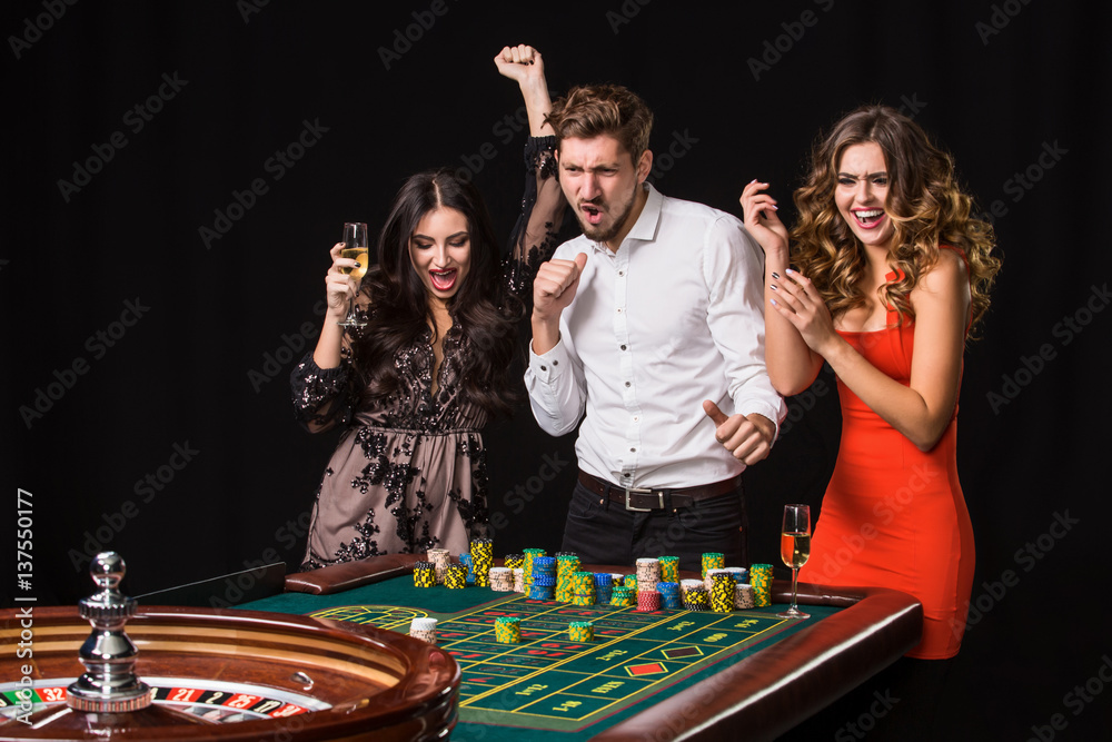 Two young women and man behind roulette table on black background Stock ...