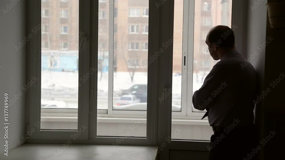 A man stands and thinks near window, he leaned against the wall, on the ...
