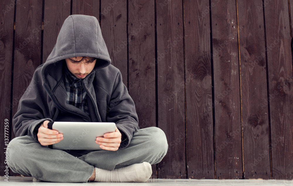 teenager with a tablet computer at the wooden walls, hacker sitting on ...