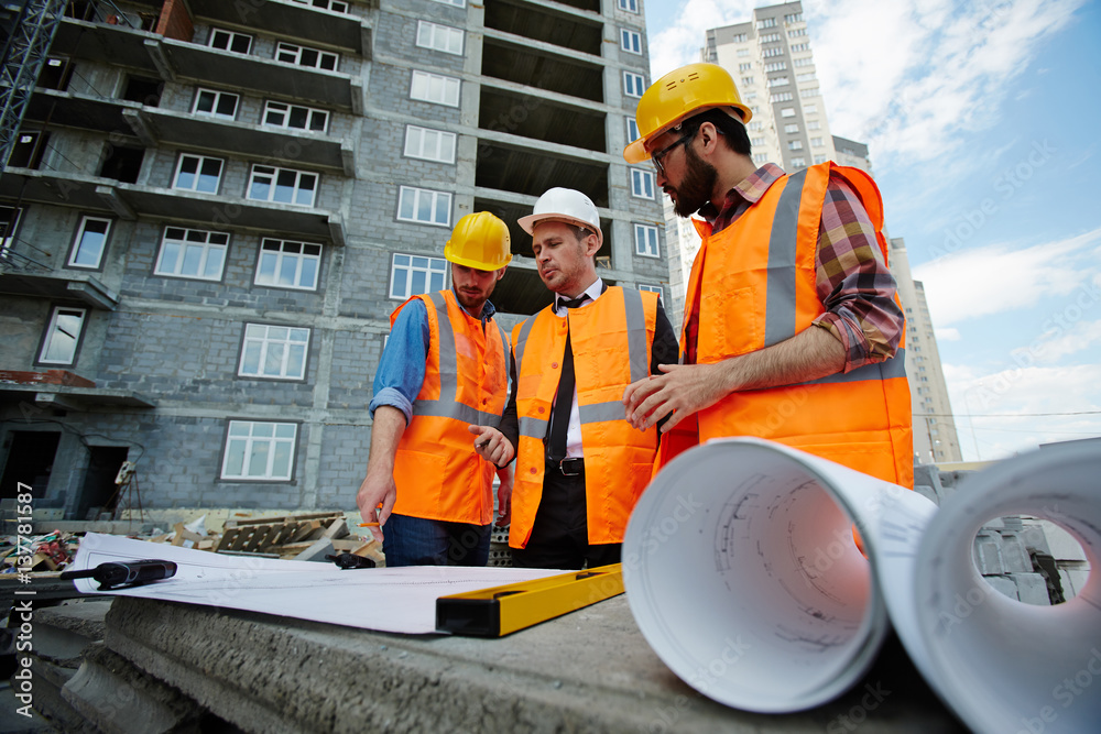 Low angle portrait of two workmen showing apartment building blueprints ...