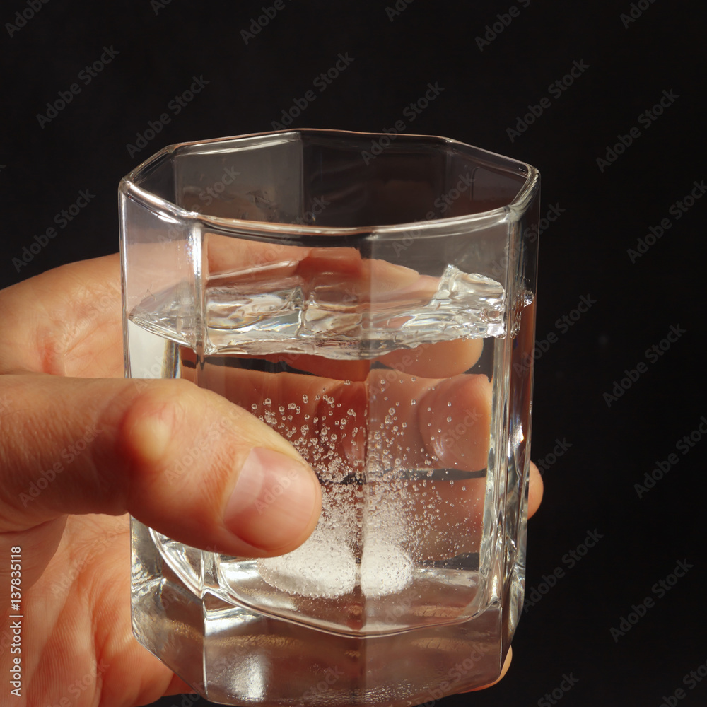 Hand with a glass of water and soluble tablet on a dark background ...