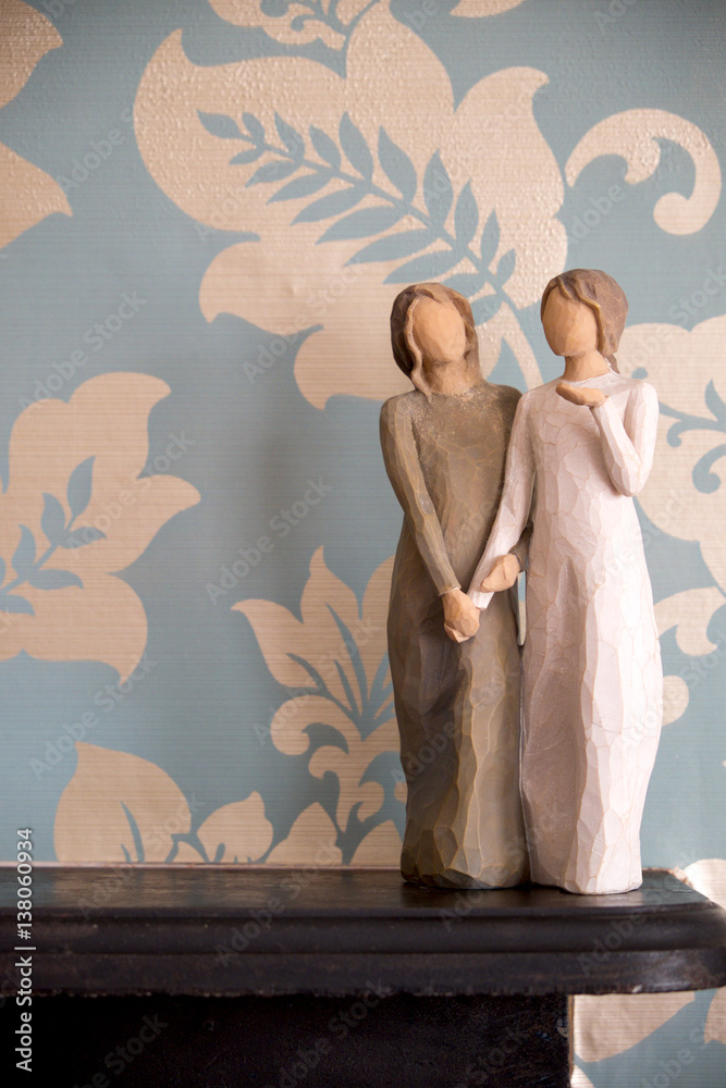 wooden statue of two women holding hands, statue is on a black ...