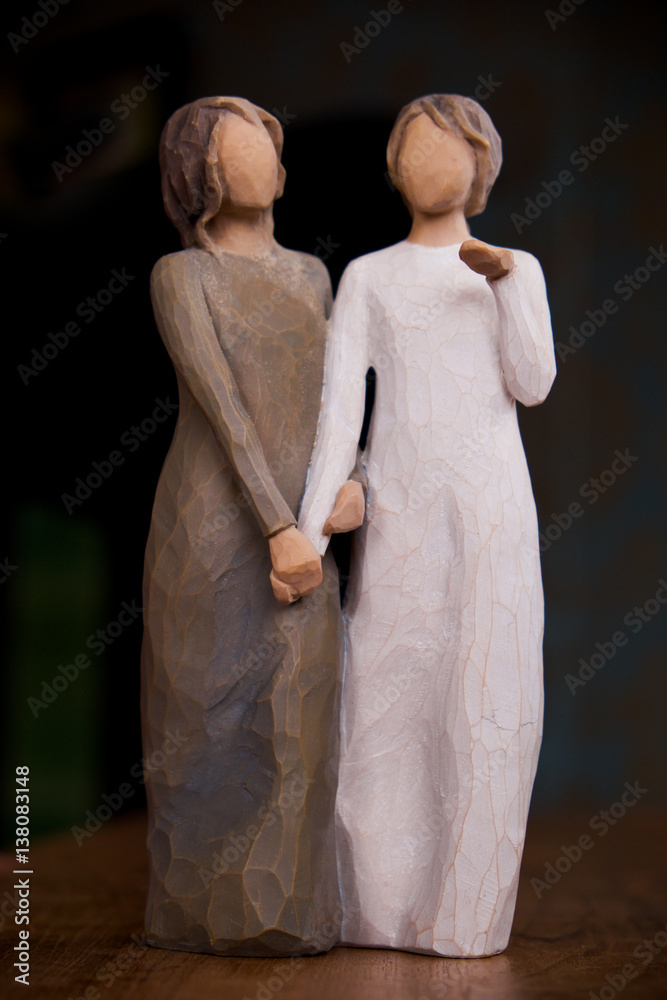 wooden statue of two women holding hands, statue is on a black ...