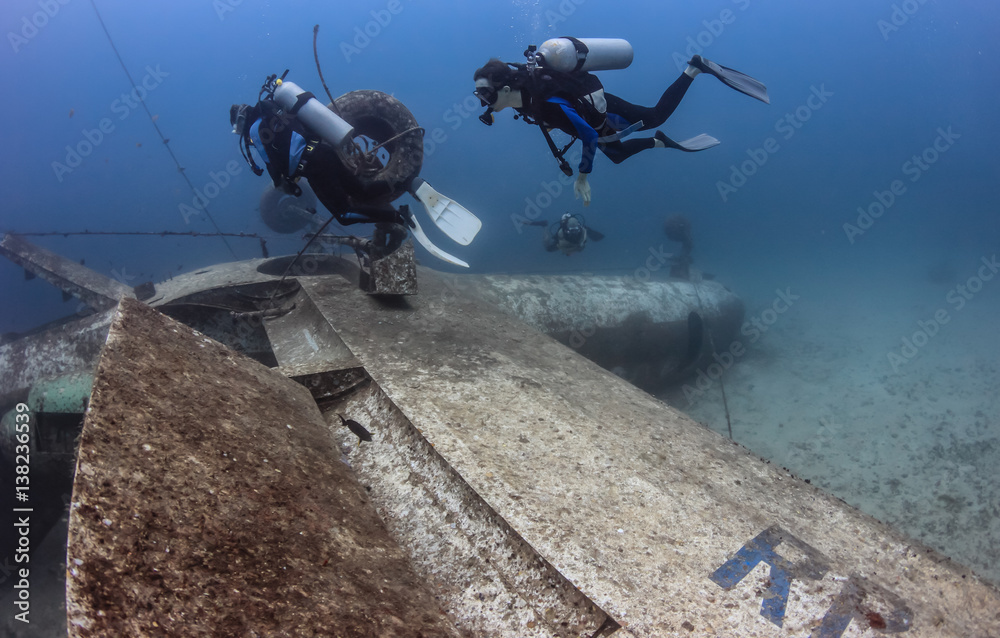 SCUBA divers over the wing of an upside down aircraft wreck on the ...