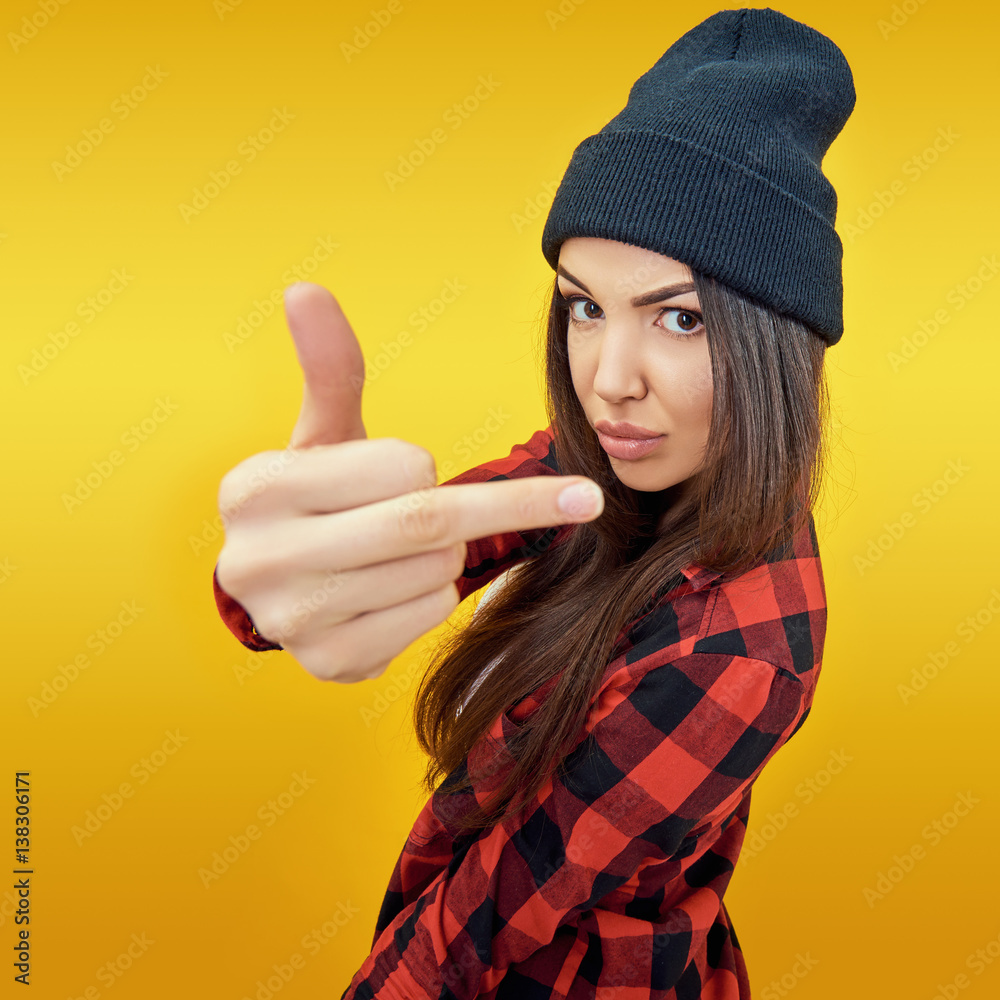 Hipster girl in jeans, checked shirt and hat showing middle fingers ...