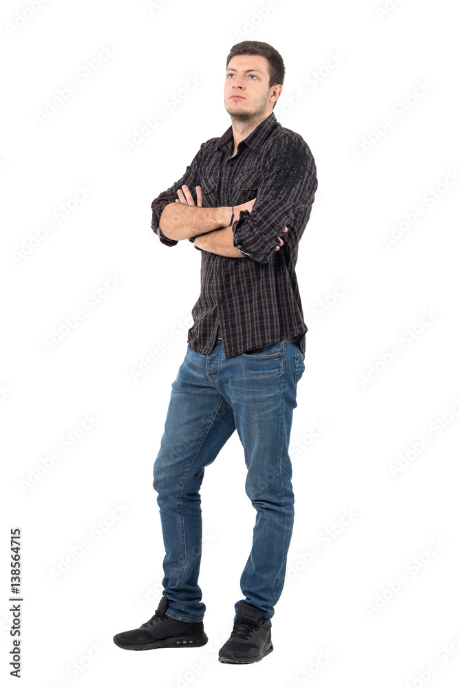 Young handsome casual man in jeans and shirt with crossed arms looking ...