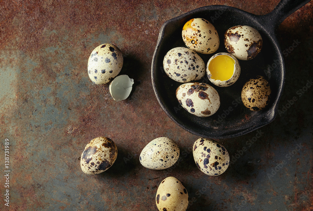 Whole and broken quail eggs with yolk in shell in small iron cast pan ...