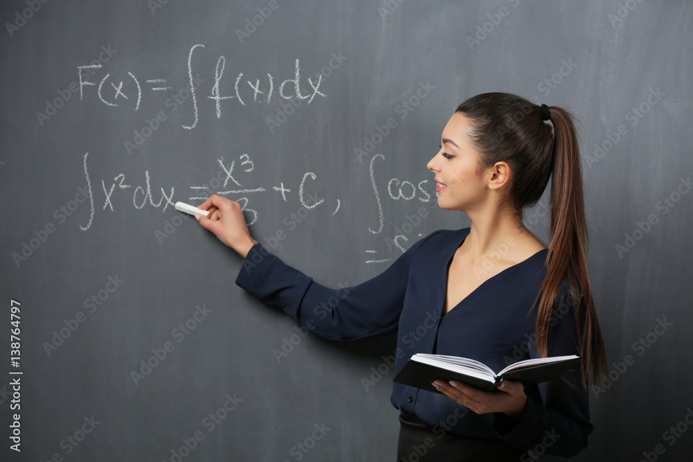 Beautiful young teacher explaining math formulas written on blackboard ...