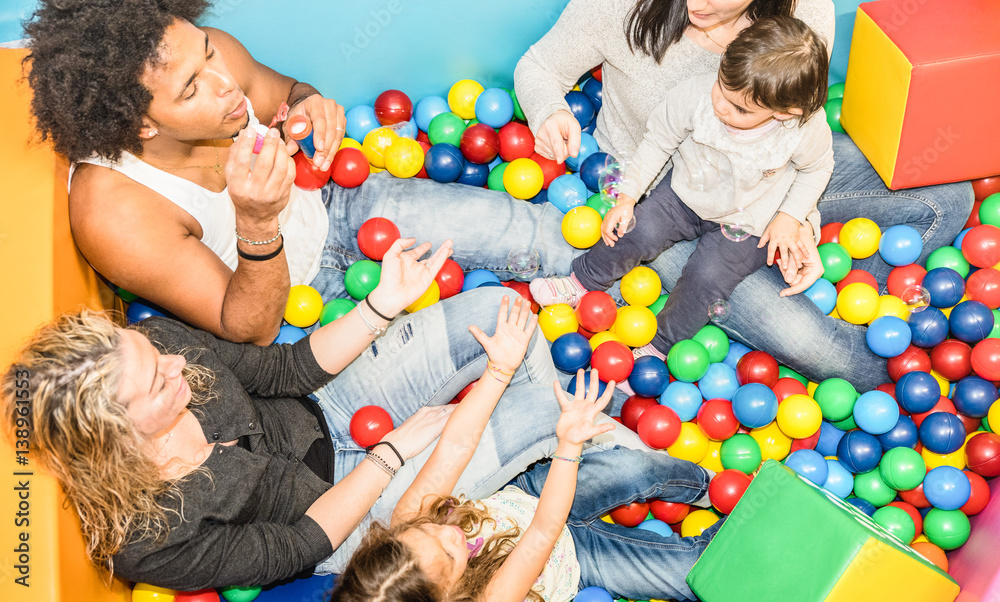 Happy multiracial mom and dad playing with daughter inside ball pit ...