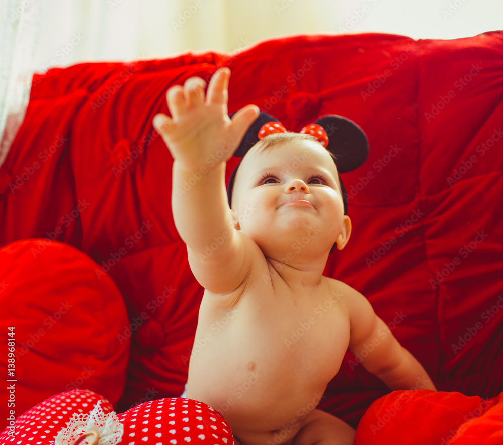Little girl in ears of Minnie Mouse raises her hand up sitting before ...
