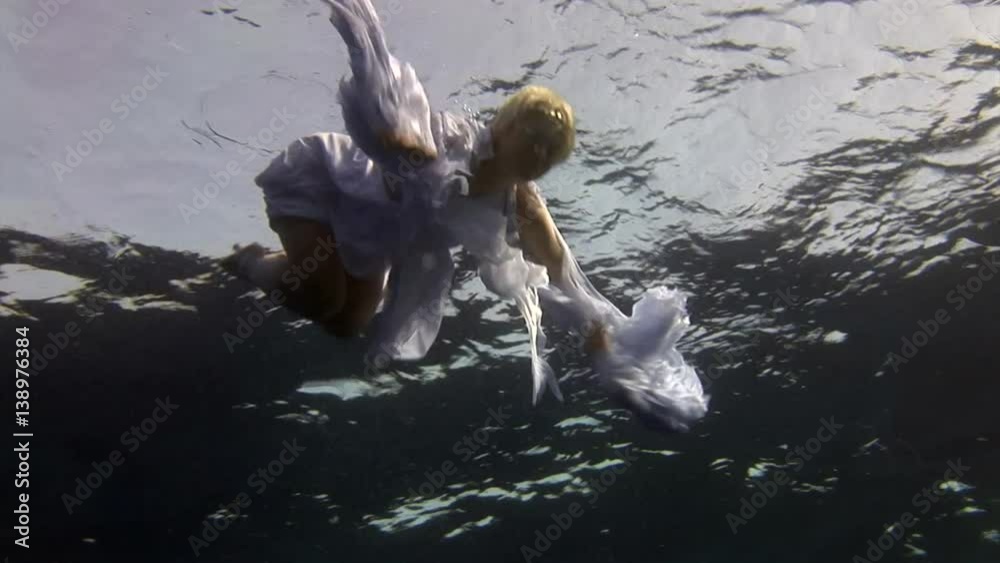 Underwater model free diver in costume angel swims in clean water in ...