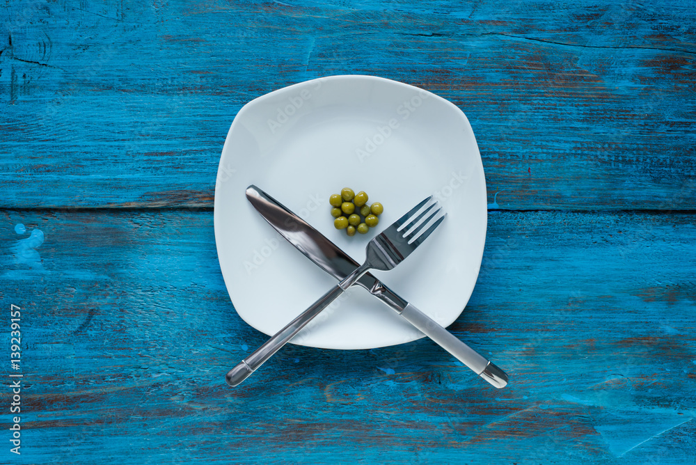 Pea, fork and knife on a large white plate. Just one little pea for a ...
