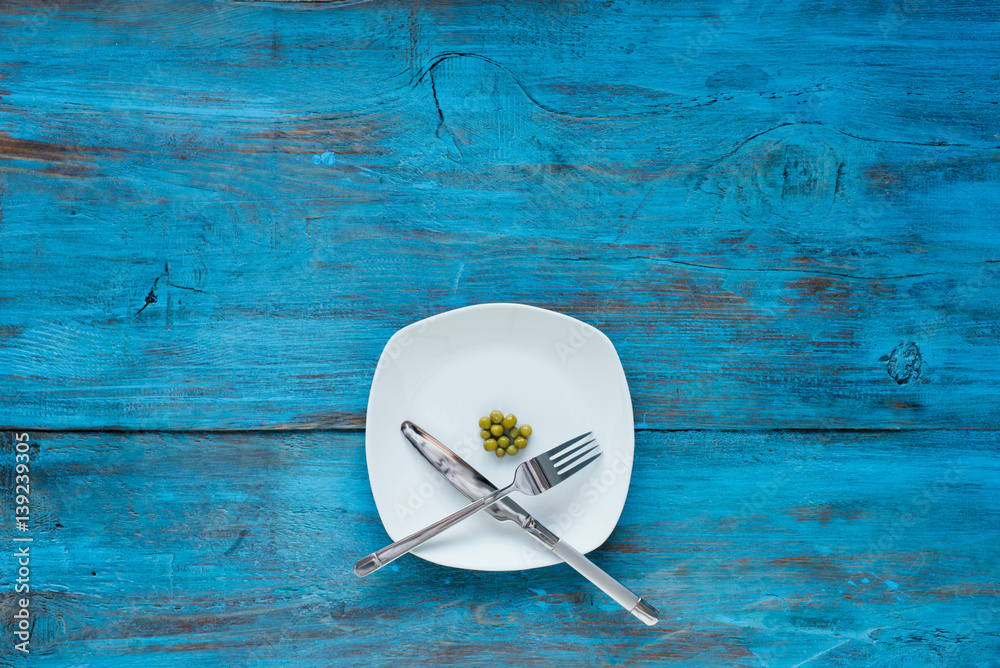 Pea, fork and knife on a large white plate. Just one little pea for a ...