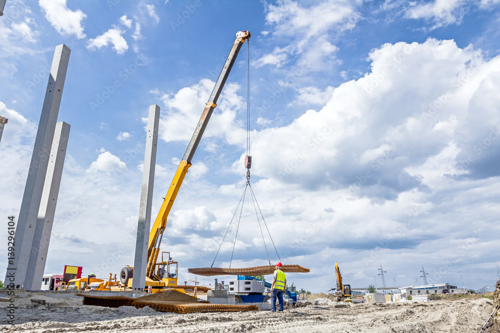 Mobile crane is carry pile of concrete armature, rusty square ...