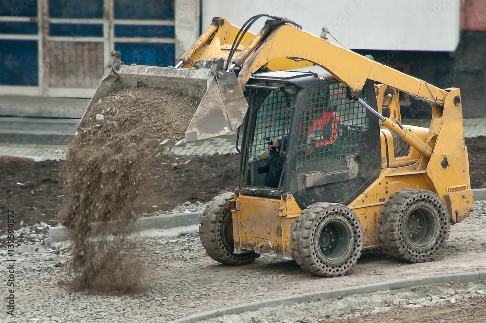 Yellow wheel skid-steer loader machine unloading gravel at construction ...
