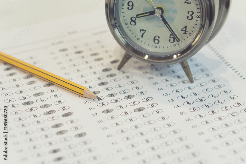 pencil sitting on a test bubble sheet and alarm clock, optical form of ...