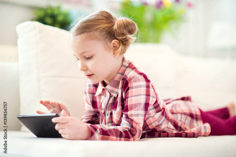 Pretty little child girl using a digital tablet, looking and smiling ...