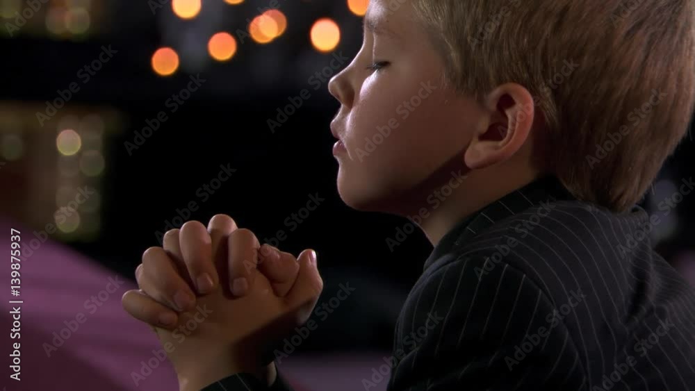 Close-up face of young boy praying with bowed head and folded hands ...